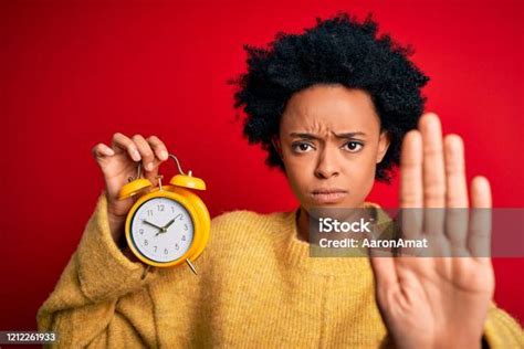 젊은 아프리카계 미국인 Afro 여자 곱슬 머리 들고 빈티지 알람 시계 와 열린 손으로 정지 기호와 심각하 고 자신감 있는 표정 방어 제스처 경계 표지에 대한 스톡 사진 및