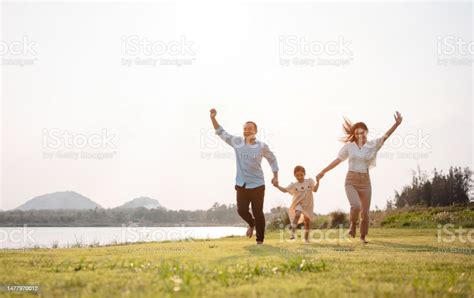 공원 일몰 빛에 행복 한 가족입니다 주말에 강이 있는 초원에서 함께 달리는 가족 부모는 아이의 손을 잡고 있습니다건강 생명 보험