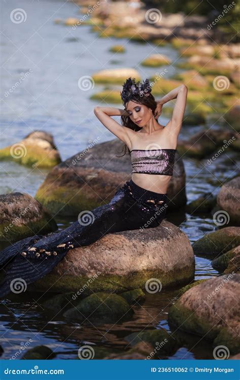 Asian Mermaid Posing At Ocean Shore On Rocks While Wearing Seashell