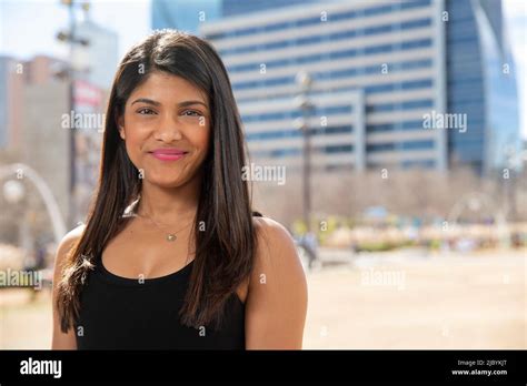 Smiling Portrait Of Young Ethnic Woman Standing In Park Wearing Black