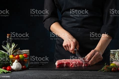요리사는 진한 파란색 배경의 검은 색 보드에 칼로 신선한 대리석 쇠고기로 자릅니다 갈비뼈 스테이크를 준비하는 무대 뒤편 음식