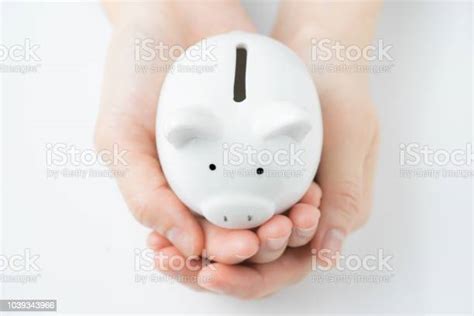 저축 하 고 미래 성장을 위한 투자 젊은 여성의 손의 상위 뷰 부드러운 부드러운 톤에 흰색 테이블에 흰 돼지 저금통을 들고