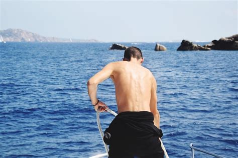 Premium Photo Rear View Of Shirtless Man On Boat In Sea Against Sky
