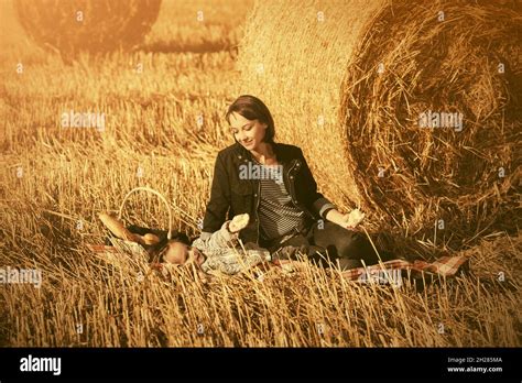 Happy Mother And Two Year Old Girl Relaxing Next To Hay Bales In Summer