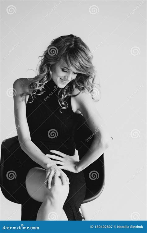 Beautiful Elegant Slim Woman In A Black Tight Fitting Dress Sits On A