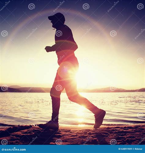 Бегун в лучах Солнця на пляже Спортсмен в бейсбольной кепке Jogging во