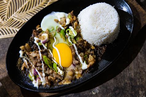 A Plate Of Sizzling Sisig With Freshly Cracked Egg And White Jasmine