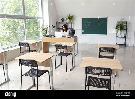 Female Asian Teacher Working With Laptop At Table In Classroom Stock Photo Alamy