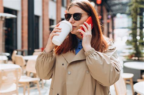 패션 사무복을 입은 행복한 쾌활한 젊은 빨간 머리 여성과 에코 차 한 잔과 전화 통화를 하고 있다 모형 스마트폰과 바이오 커피잔을 들고 있는 여자 도시 개념 거리에 대한