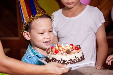 귀여운 아시아 아이 소년은 그의 어머니가 그에게 주는 맛있는 생일 케이크와 함께 놀랍습니다 파티에서 생일 케이크에 촛불을 불고
