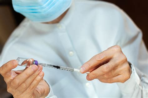 흰색 수술 가운과 파란색 마스크를 입은 의사가 당뇨병을 위한 인슐린이 있는 의료용 주사기와 병을 손에 쥐고 있습니다 설탕 중독