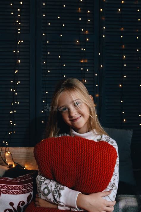 Девушка в свитере сидя на кровати и обнимая красную подушку Стоковое Изображение изображение