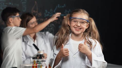 Caucasian Girl Showing Thumb While Teacher Doing Experiment Behind