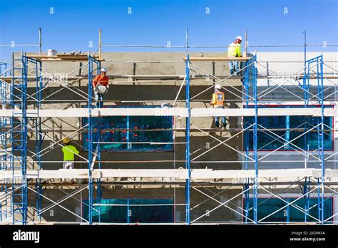 Four Construction Workers On Scaffolding Installing Stucco To The Outside Of A Commercial