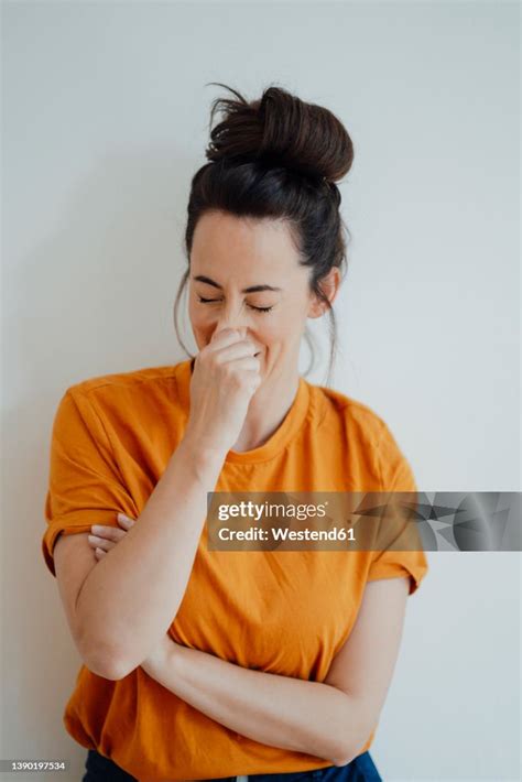 Playful Woman Pressing Nose Standing In Front Of White Wall High Res