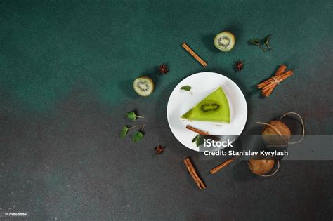 녹색 배경에 흰색 접시에 키위를 곁들인 수제 치즈 케이크 키위 조각 계피 스틱 및 민트 잎으로 장식되었습니다 상위 뷰 0명에