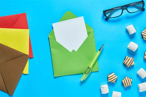 흩어져있는 줄무늬 사탕 빈 종이 시트 안경 펜이있는 녹색 봉투 근처의 마시멜로가 파란색 책상위에 놓여 있습니다 러브 레터 컨셉