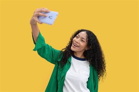 아프리카계 미국인 여성은 밝은 노란색 배경에 고립된 쾌활한 셀카를 찍으면서 행복과 자신감을 발산한다 무선 기술을 통한 소통과 축하의 전형을 보여줍니다 스마트 폰과 함께하는