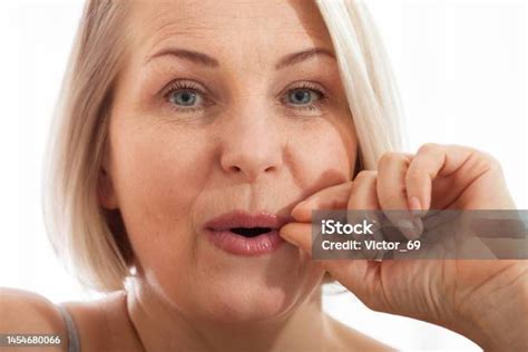 50대 중년 노인이 흰색 배경에 고립된 카메라를 바라보고 있다 입술을 가진 여자는 조용히 침묵하라는 표시를 보여줍니다 50 54