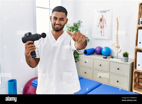 Young Indian Physiotherapist Holding Therapy Massage Gun At Wellness