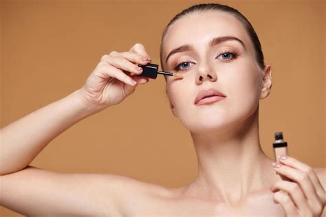 Premium Photo Woman Applying Concealer Under Her Eyes On Beige Background
