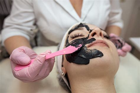 스파 살롱에서 젊은 예쁜 여자 얼굴에 검은 마스크를 적용하는 미용사 가꿔주기에 대한 스톡 사진 및 기타 이미지 가꿔주기