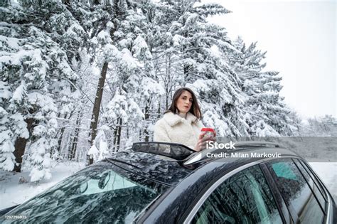 아름다운 젊은 여성이 눈 덮인 숲을 통과하는 길에 쉬고 차의 선루프를 통해 서있는 아름다운 자연을 관찰합니다 겨울 방학 30