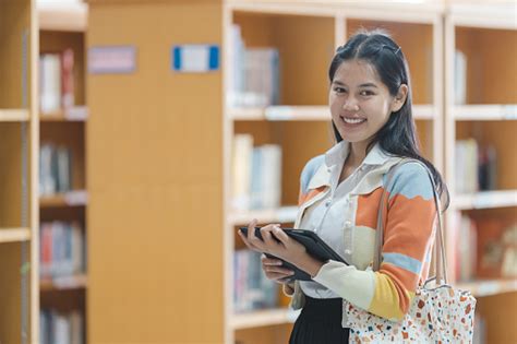 대학 이나 대학 도서관에서 똑똑하고 행복한 포즈로 태블릿을 들고 유니폼을 입은 젊은 아시아 여성 학생 기술 학습 개념으로 청소년