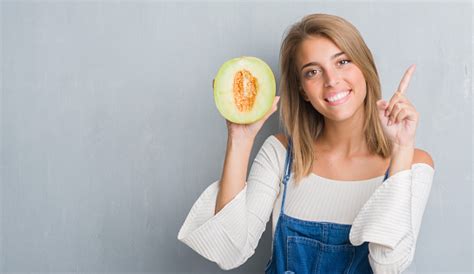 그런 지 회색에 아름 다운 젊은 여 자가 놀 생각으로 신선한 멜론 멜론을 들고 벽 또는 행복 한 얼굴 넘버 원 가리키는 손가락 질문 가리키기에 대한 스톡 사진 및 기타