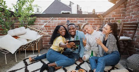 쾌활한 젊은 남녀들이 개방형 테라스에서 함께 휴식을 취하면서 현대 스마트폰으로 셀카를 찍고 있다 다문화 친구들은 맛있는 간식과 알코올 음료로 파티 시간을 보냅니다 사진