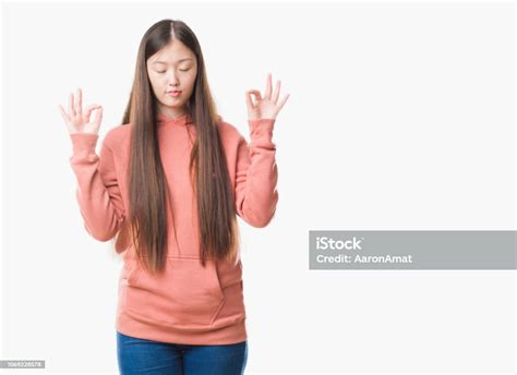 스포츠 Sweathshirt를 착용 하는 고립 된 배경 위에 젊은 중국 여자 휴식과 명상 손가락으로 제스처를 하 고 폐쇄 눈으로 웃 고 요가 개념 갈색 머리에 대한 스톡