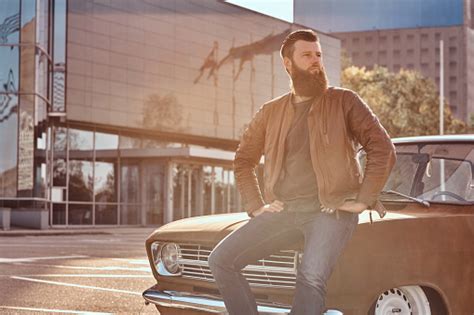 밝은 석양에 마천루 근처 도시 주차장에서 조정 복고풍 자동차에 기대어 세련 된 남성 가을에 대한 스톡 사진 및 기타 이미지 가을 가죽 가죽 재킷 Istock