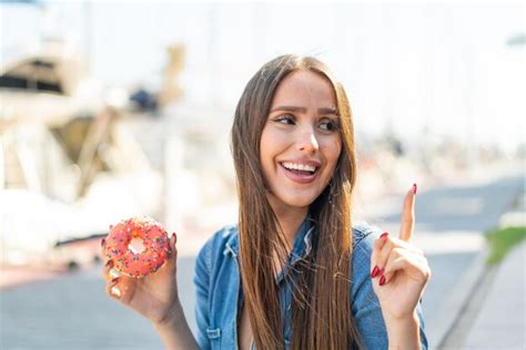 Premium Photo Young Woman Holding A Donut At Outdoors Intending To