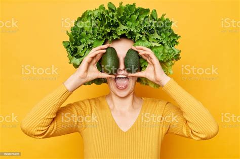 영양가 있는 음식 선택 머리에 녹색 채소를 얹은 상추 헤어 스타일을 하고 놀란 흥분한 여자가 노란색 배경 위에 고립되어 아보카도