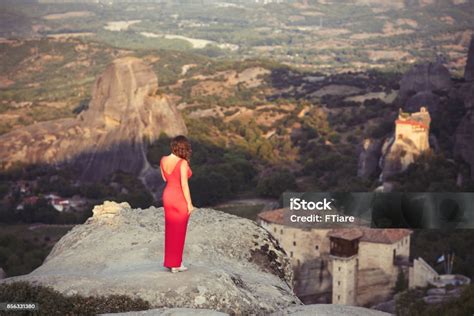 빨간 드레스에 외로운 소녀 바위의 가장자리에 앉아와 메 테오 라의 수도원에서 보인다 바위와 그리스 테 살 리에 유성의 수도원에