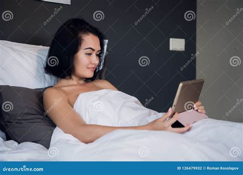 Portrait Of Happy Young Caucasian Woman Sitting In Bed Using Digital