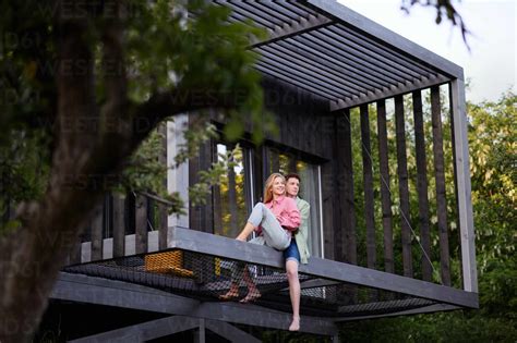 A Young Couple Sitting And Cuddling In Hammock Terrace In Their New