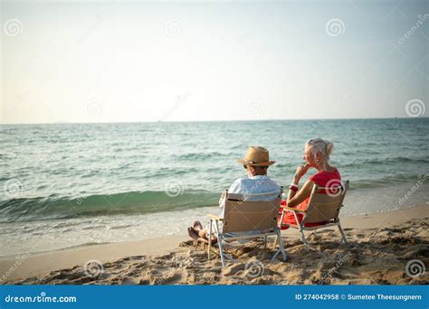 A Couple Of Elderly Sitting In Chairs At The Beach Watching The Sun And