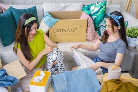 기부를 위해 옷을 정리하고 아늑한 거실에서 두 명의 여성이 물건을 분류하고 있습니다 그들은 미소를 지으며 자선 활동에 참여하고 있으며 다양한 의류 품목과 기부 상자에