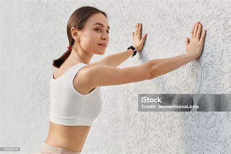 흰색 스포티 한 상의를 입고 야외에서 가벼운 벽에 기대어 스포츠 운동 후 포즈를 취하는 갈색 머리 여성의 측면 보기 초상화 25 29세에 대한 스톡 사진 및 기타 이미지