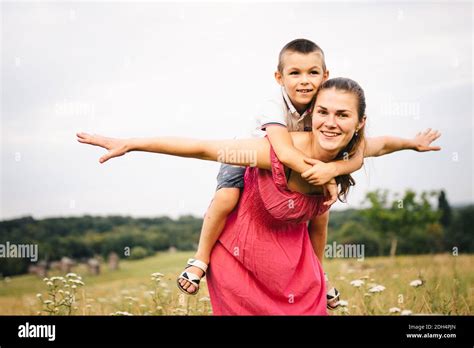 Woman Playing With Little Son In Field With Weeds And Meadow Flowers On