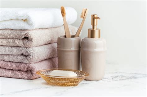 빈티지 황금 목욕은 비누와 칫솔 옆에 깨끗하고 부드러운 수건을 쌓아 놓습니다 흰색 분홍색 베이지색 수건과 흰색 배경에 욕실 액세서리가 있습니다 개념에 대한 스톡 사진 및