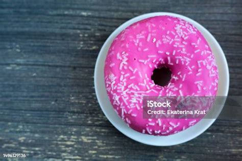 하얀 둥근 접시와 오래된 나무 회색 배경에 밝은 분홍색 도넛을 올려 놓으십시오 격리된 개체가 닫힙니다 아침 식사로 전통적인 미국 과자 복사 공간 위에 흰 설탕 장식입니다 0