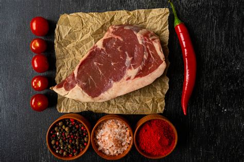 세 가지 향신료 토마토 고추 향신료 히말라야 소금 3 개의 항아리와 함께 나무 테이블에 공예 종이에 Ribeye 쇠고기 고기의 원시 조각 신선한 음식 바베큐를위한 모든 것