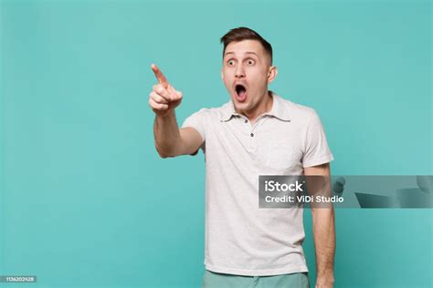 입이 열린 입을 유지 캐주얼 의류에 충격 젊은 남자 지시 검지 손가락 따로 스튜디오에서 파란색 청록색 벽 배경에 고립 사람들은