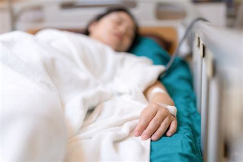 아시아 환자 여성은 병원 병동에서 손에 식염수와 주사기 라인으로 침대에 누워 있습니다 손을 들어 침대 가장자리의 레일을
