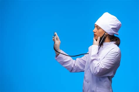 흰색 제복을 입은 젊은 간호사는 청진기로 환자를 확인합니다 무료 사진