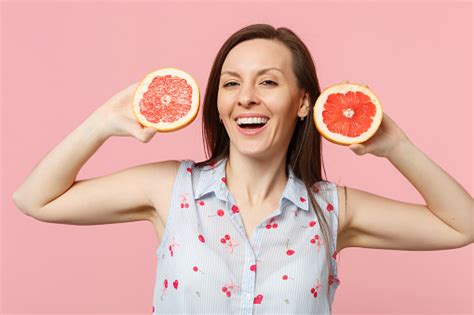 스튜디오에서 분홍색 파스텔 벽 배경에 고립 된 신선한 익은 자 몽의 Halfs를 들고 여름 옷에 아름 다운 젊은 여자 사람들은 생생한 라이프 스타일 휴식 휴가 개념입니다