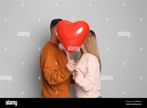 Lovely Couple Kissing Behind Heart Shaped Balloon On Grey Background