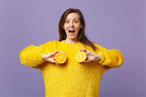 모피 스웨터에 흥분 젊은 여성은 보라색 파스텔 배경에 고립 된 신선한 잘 익은 오렌지 과일의 Halfs 유지 입을 열어 사람들은 생생한 라이프 스타일 휴식 휴가 개념입니다